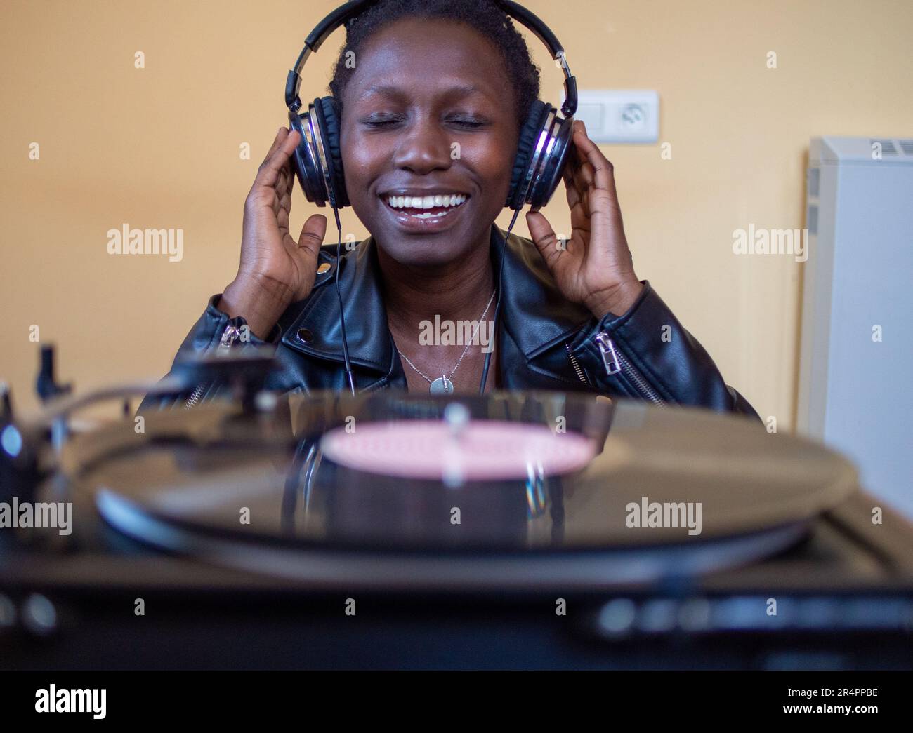 young woman wearing a leather jacket using headphones while playing a ...