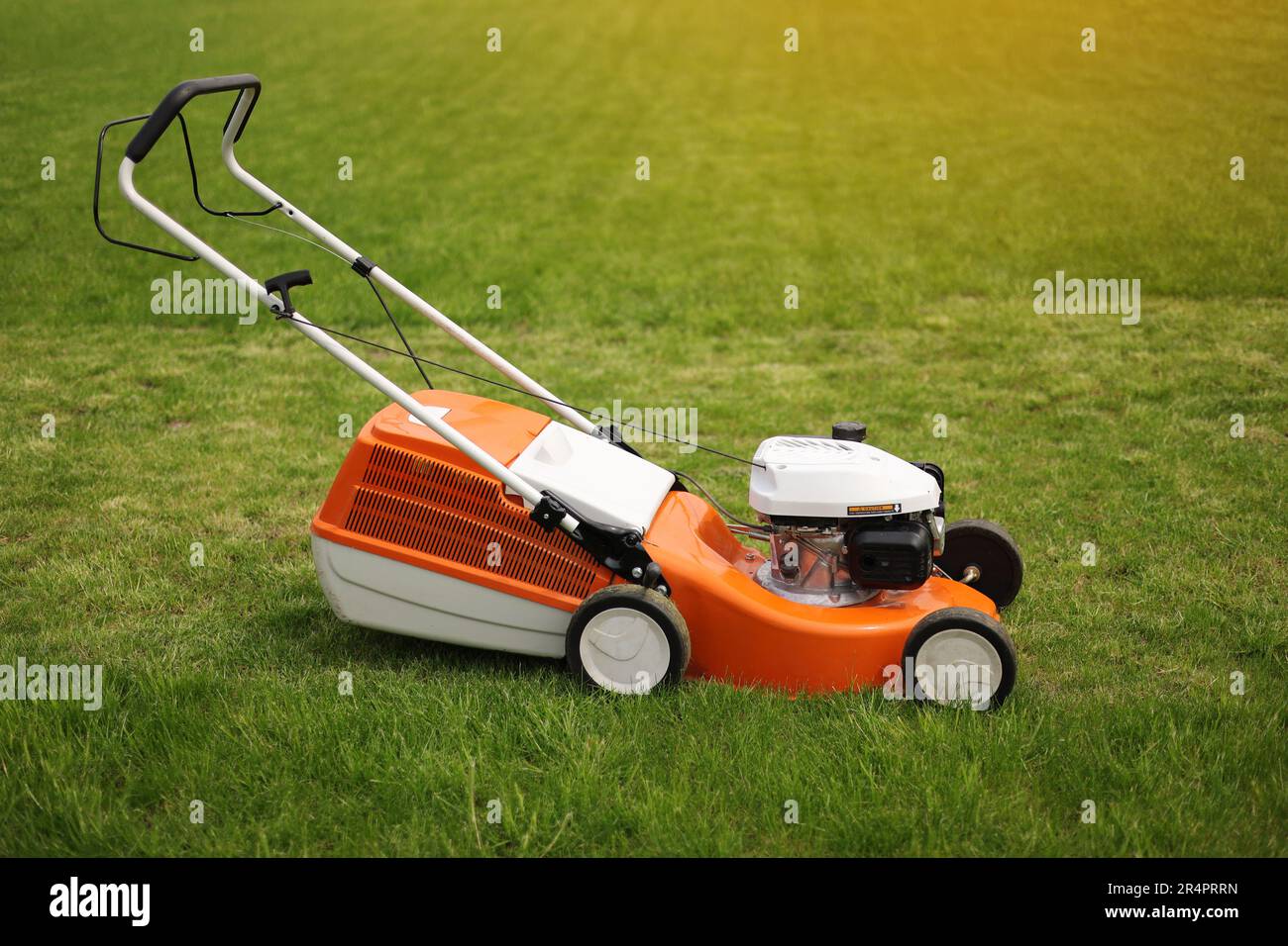 Modern orange-grey electric lawn mower on bright lush green lawn at ...