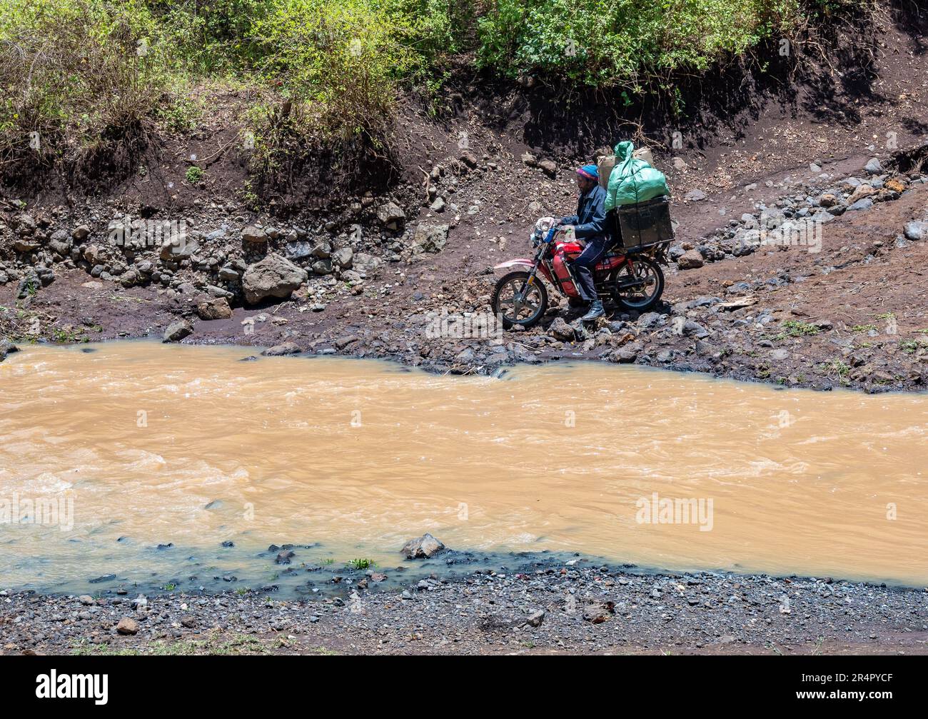 A local man on heavily loaded motorbike trying to cross a river. Kenya ...