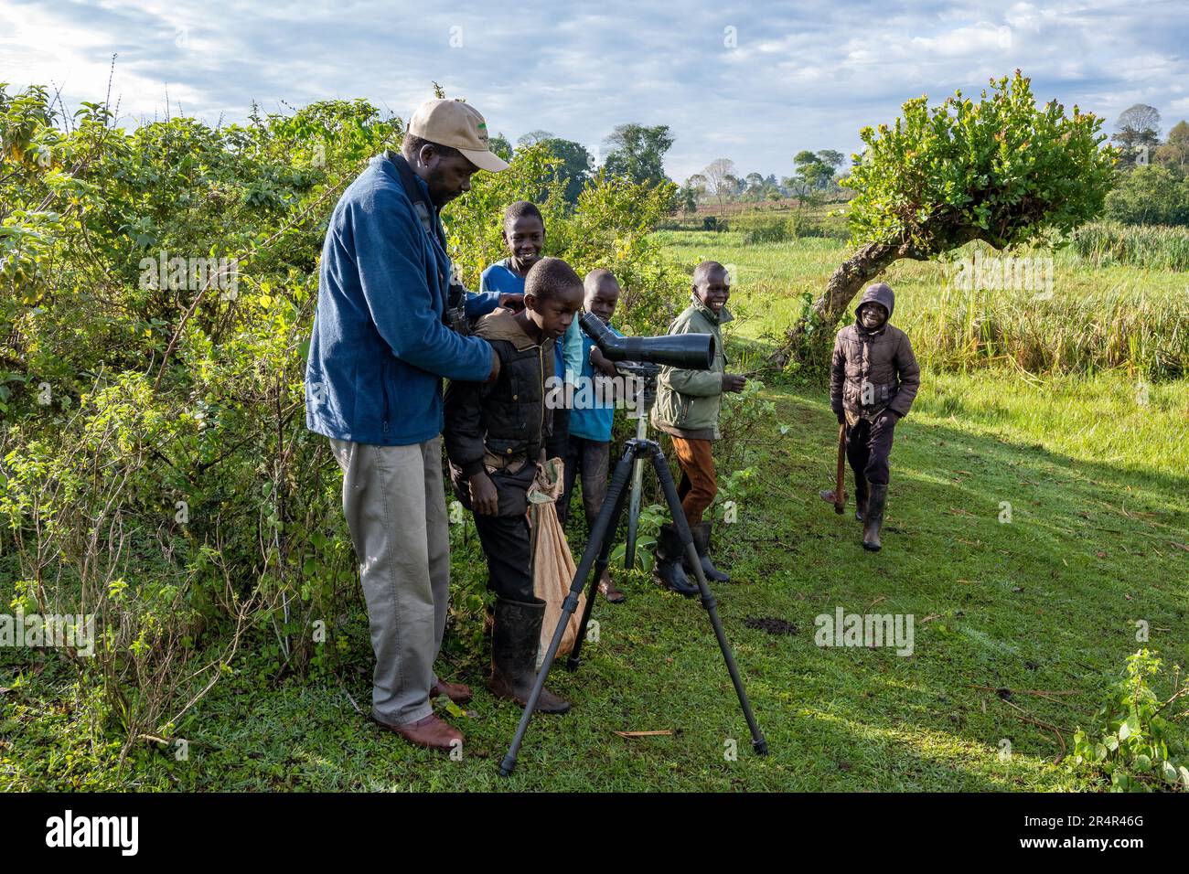 A male naturalist teaching local boys bird watching through a scope ...