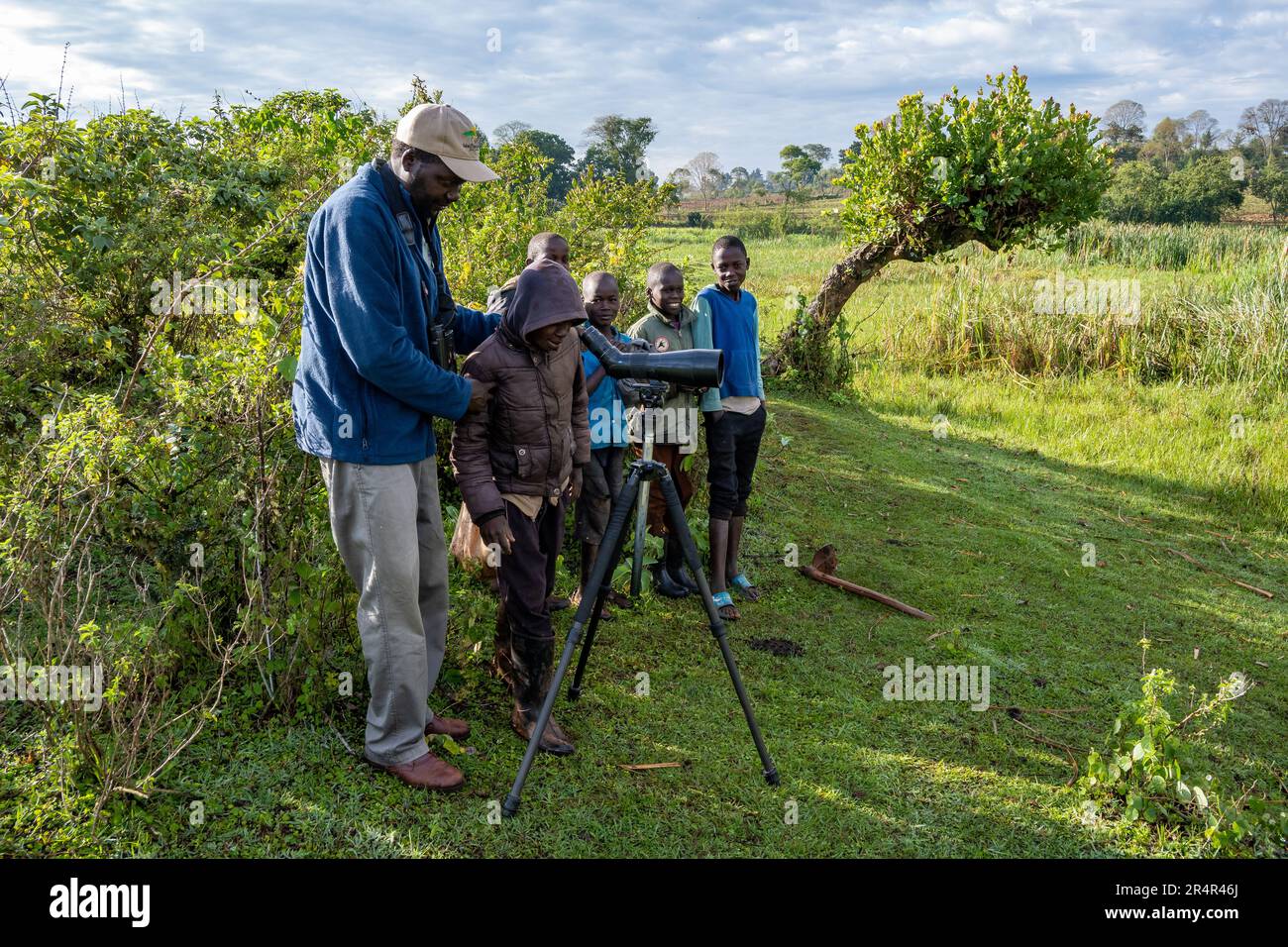 A male naturalist teaching local boys bird watching through a scope ...