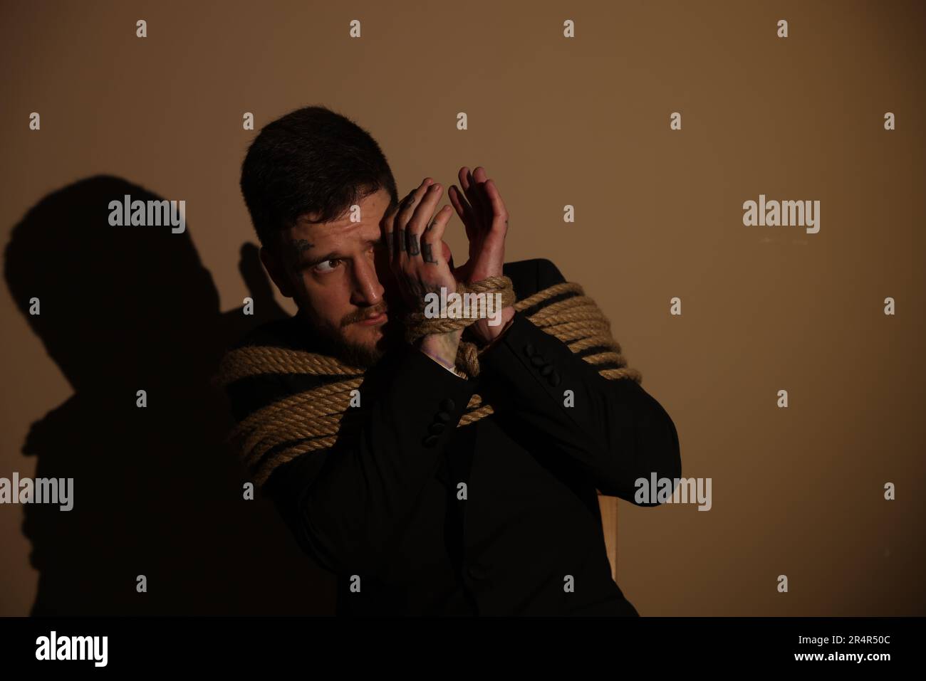 Scared man tied up and taken hostage on dark background. Space for text ...