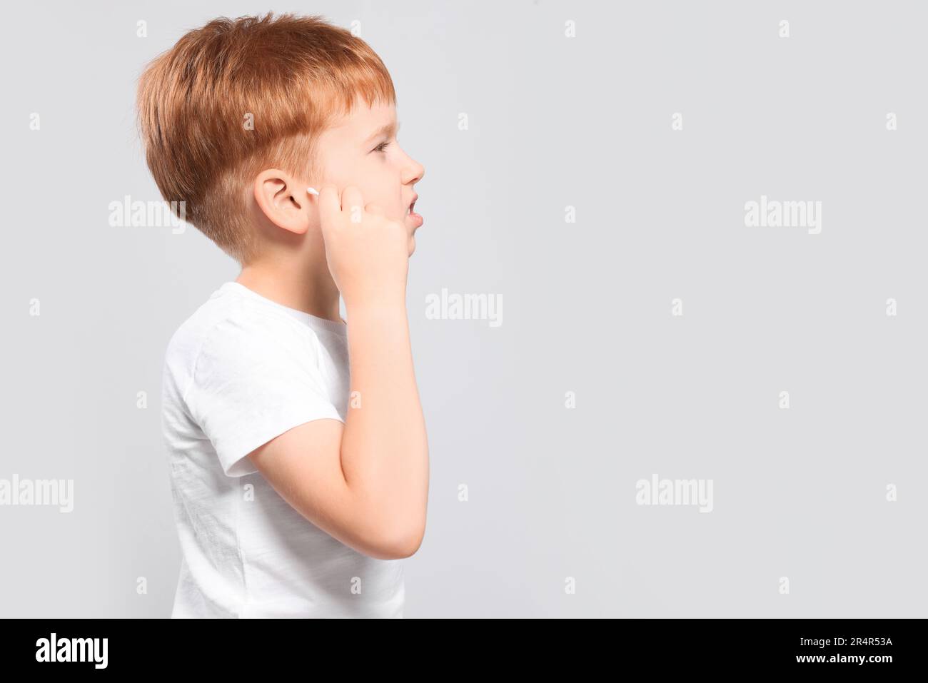 Little boy cleaning ear with cotton swab on light grey background ...