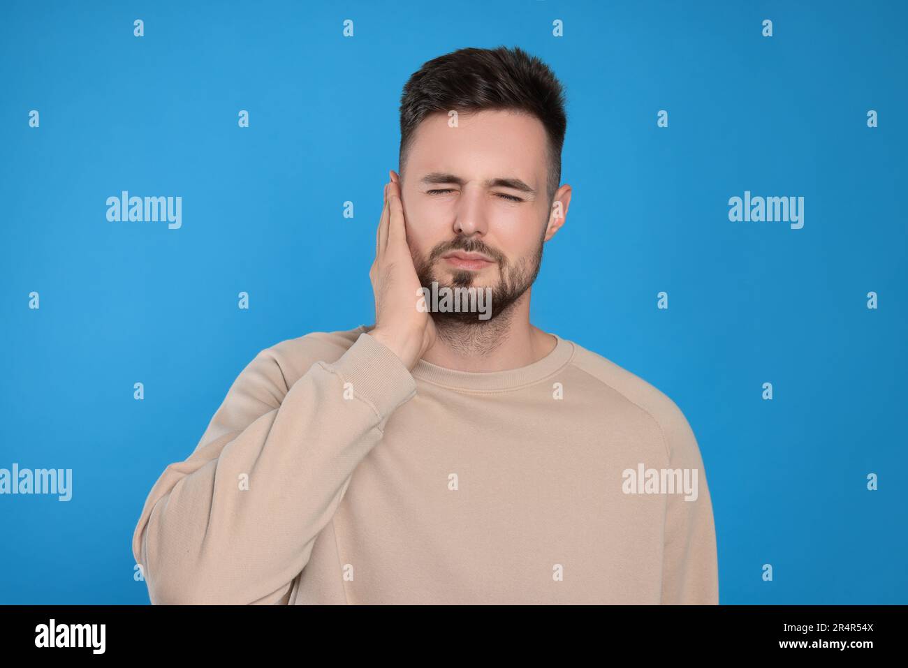 Young man suffering from ear pain on light blue background Stock Photo ...