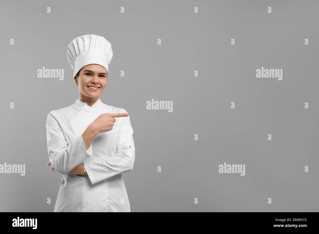 Happy female chef pointing at something on light grey background. Space ...