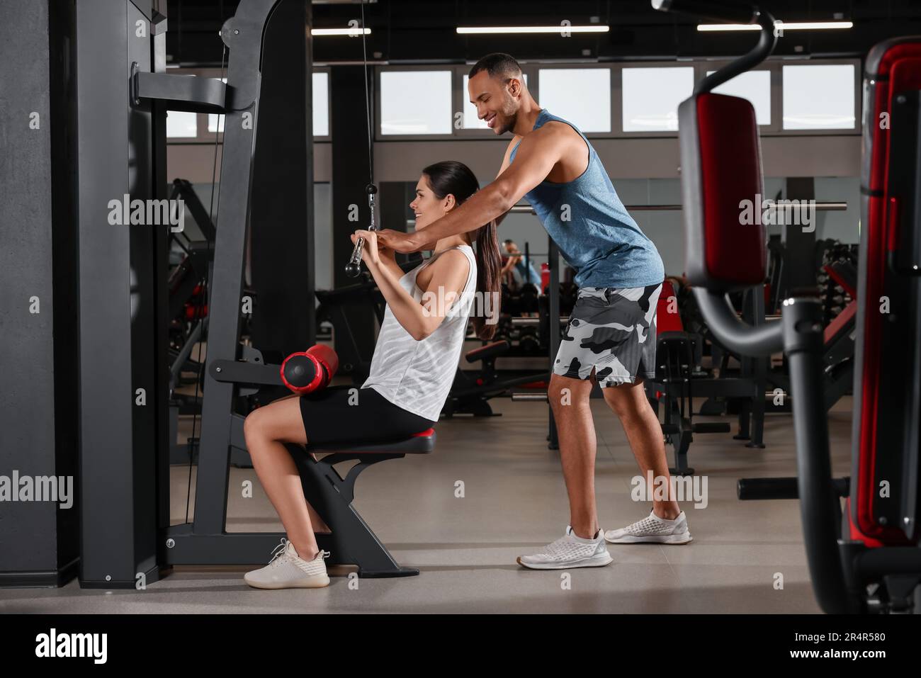 Happy trainer showing woman how to do exercise properly in modern gym ...