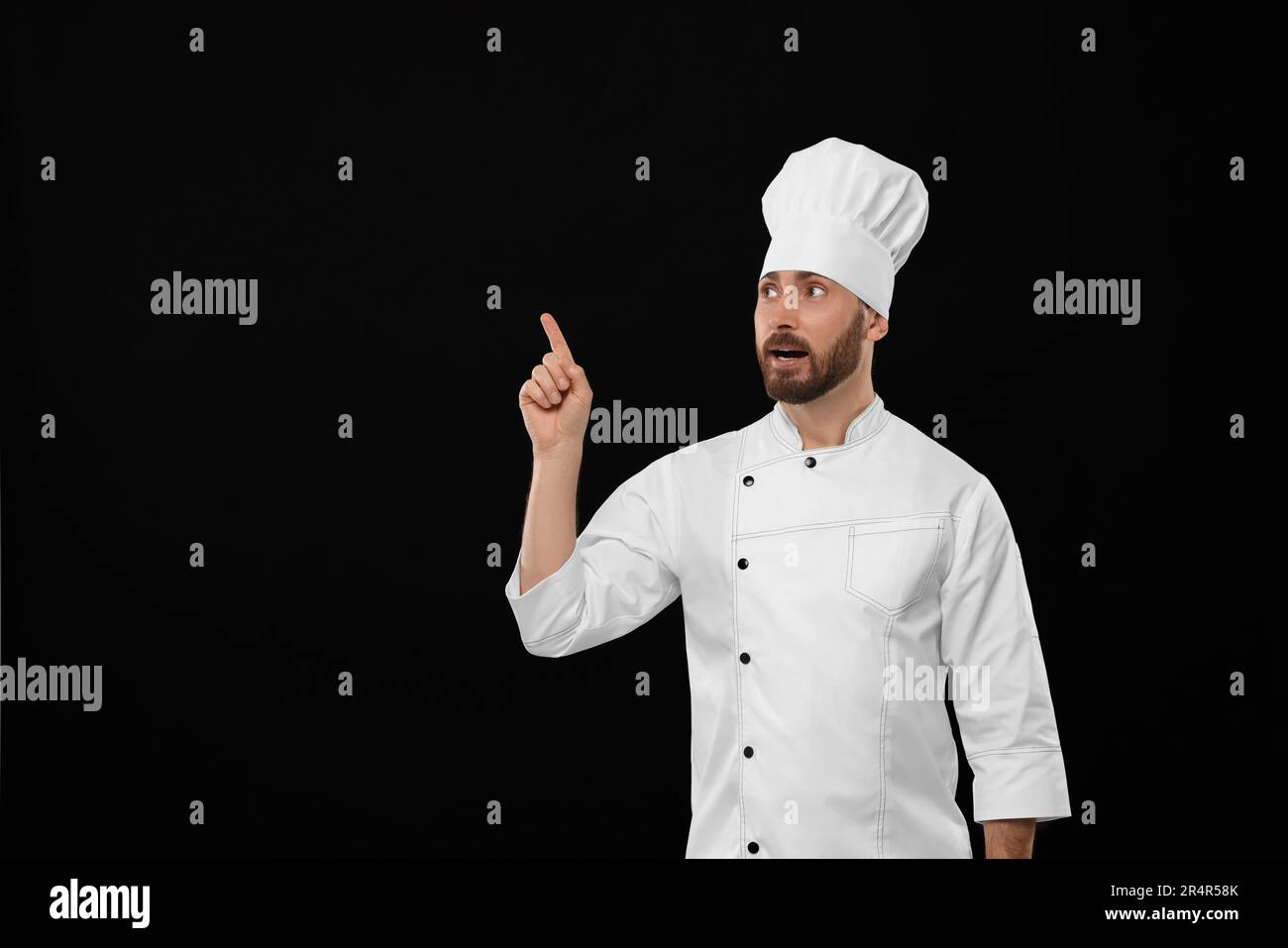 Mature chef pointing at something on black background, space for text ...