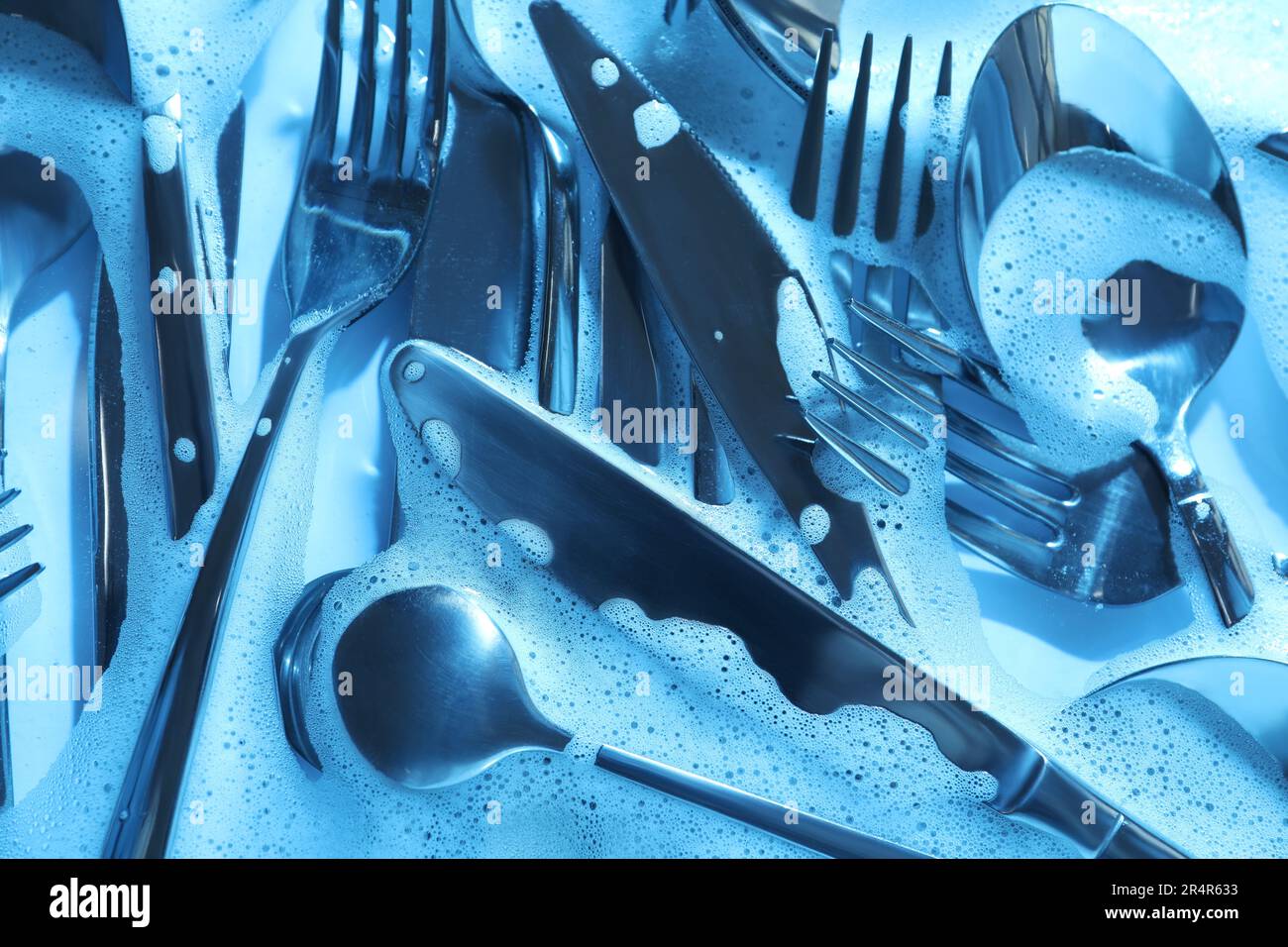 Different silverware in foam, flat lay. Toned in blue Stock Photo - Alamy