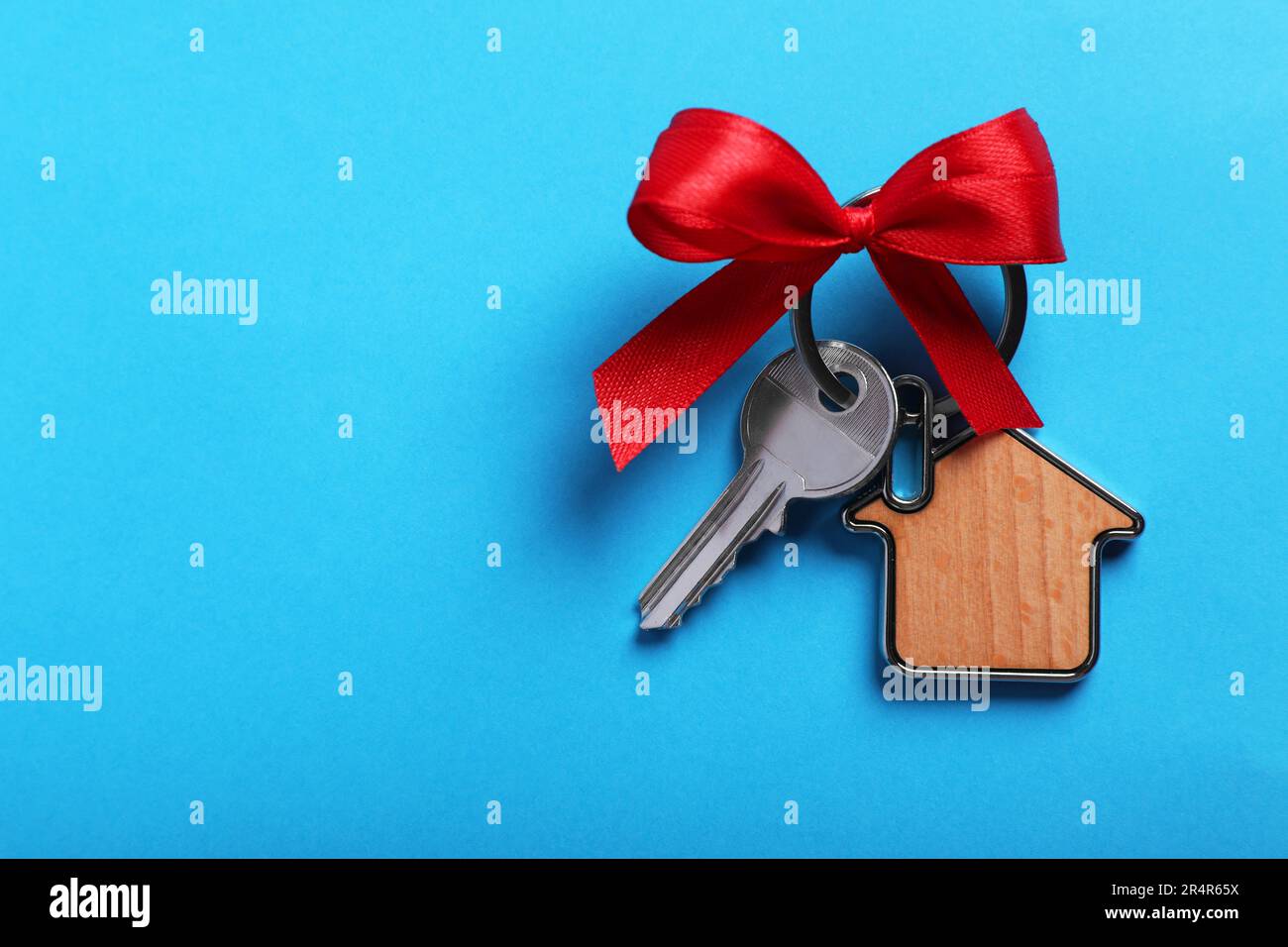 Key with trinket in shape of house and bow on light blue background ...