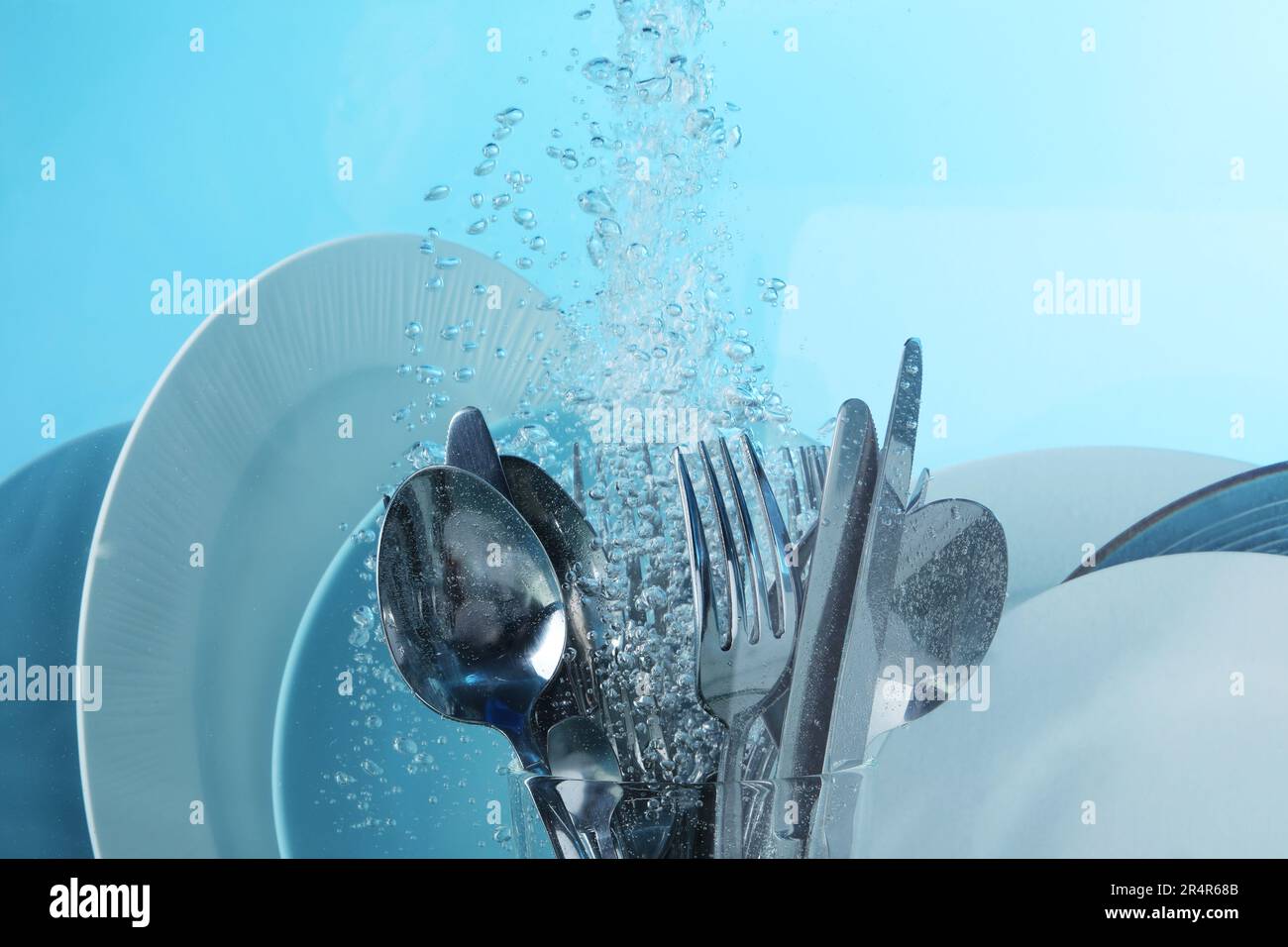 Washing silver cutlery and plates in water on light blue background ...