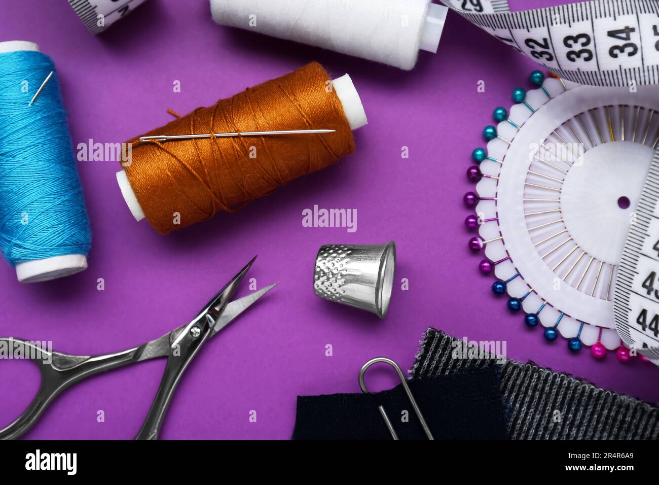 Flat lay composition with thimble and different sewing tools on purple ...