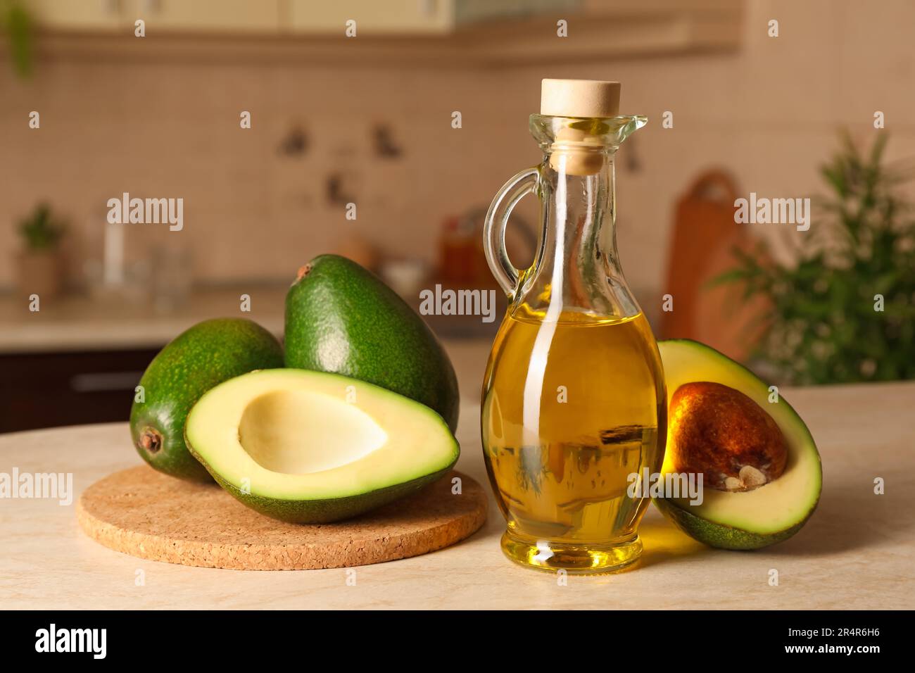 Fresh avocados and jug of cooking oil on beige marble table in kitchen ...