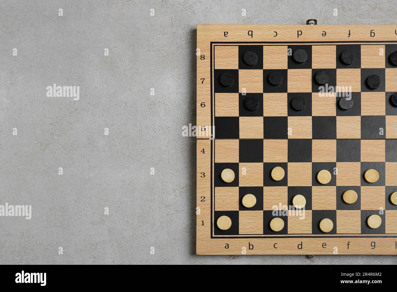 Wooden checkerboard with game pieces on light grey background, top view ...