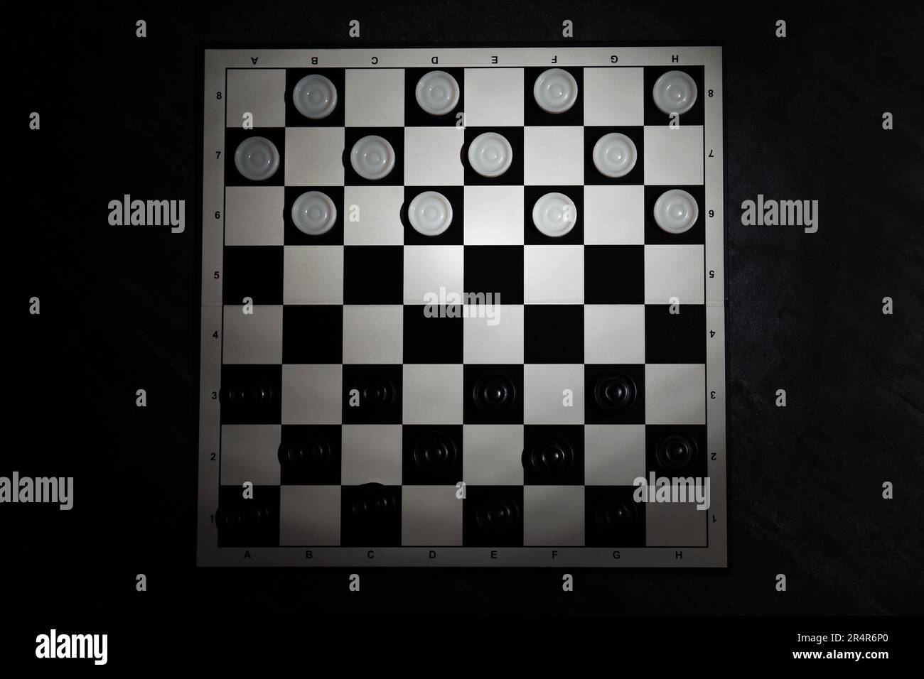 Checkerboard with game pieces on black table, top view Stock Photo - Alamy