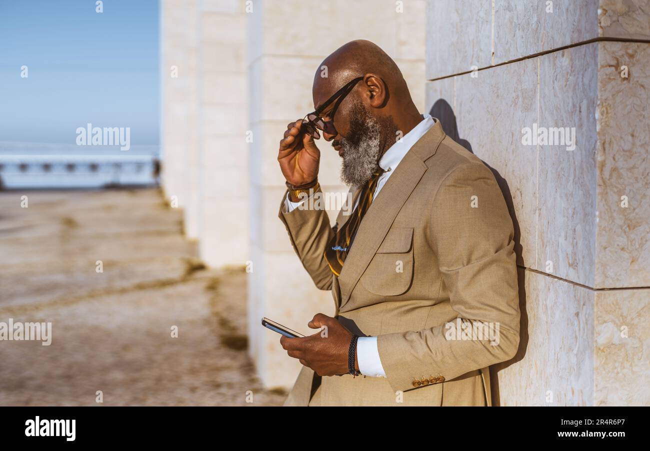 Outdoors, a thoughtful African businessman stands by a limestone pillar ...