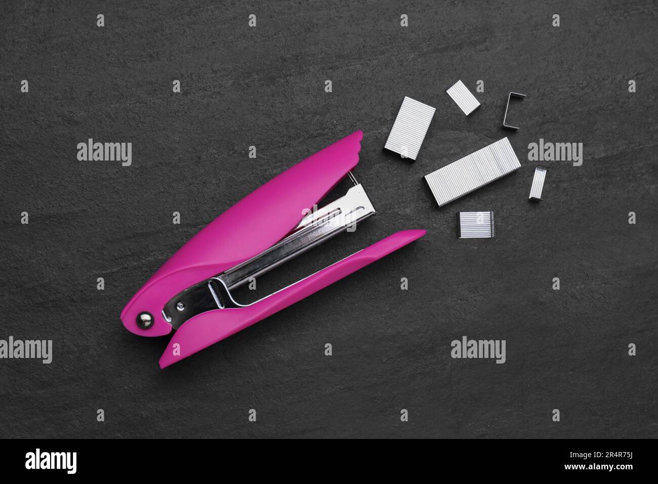 New bright stapler with staples on black table, fat lay. School ...