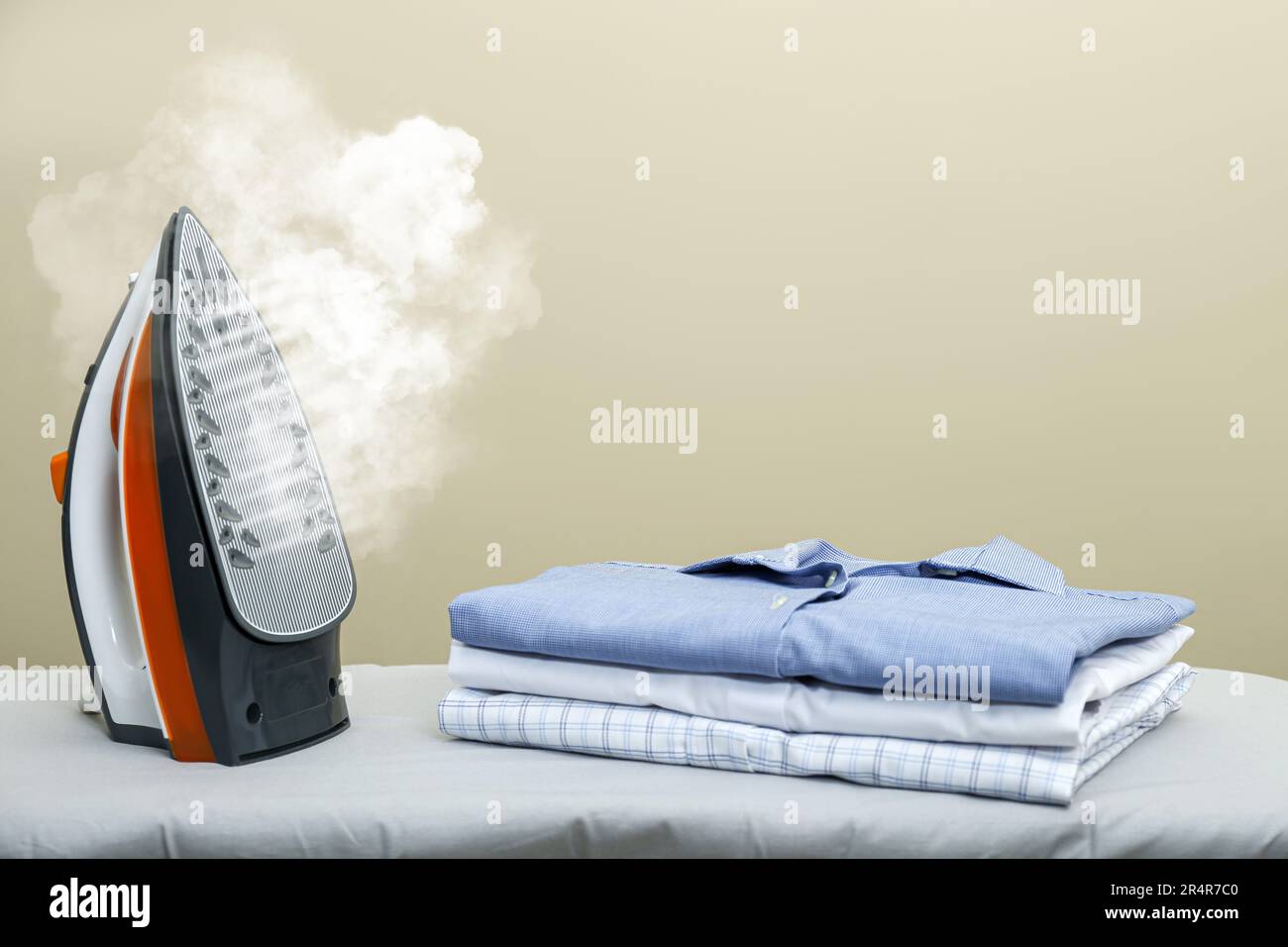Modern iron with steam and folded clothes on ironing board, space for ...