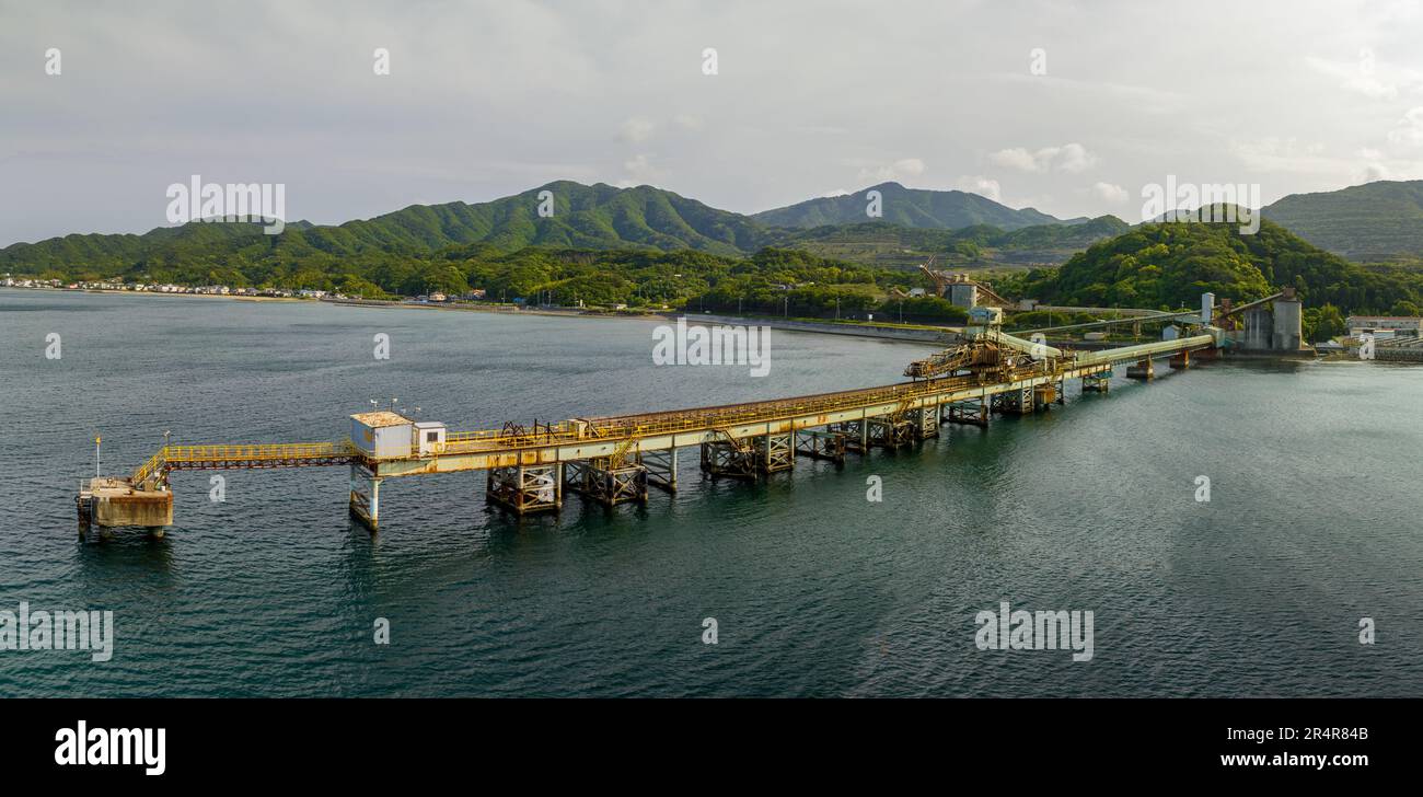 Long loading pier with rusted and equipment stretches into sea on coast ...
