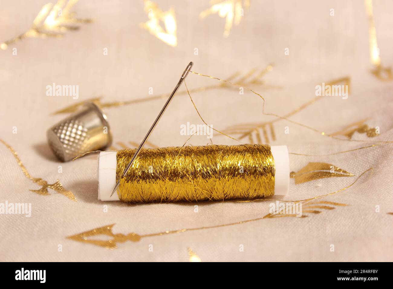 Spool of Gold Thread With Thimble on Metallic Chiffon Fabric Stock ...