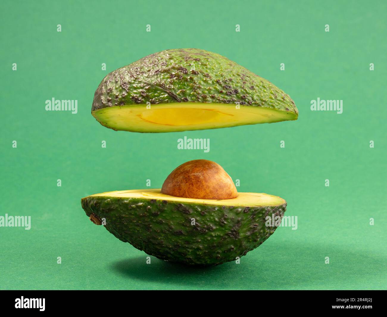 Two halves of a green avocado and the core of the fruit float in the ...