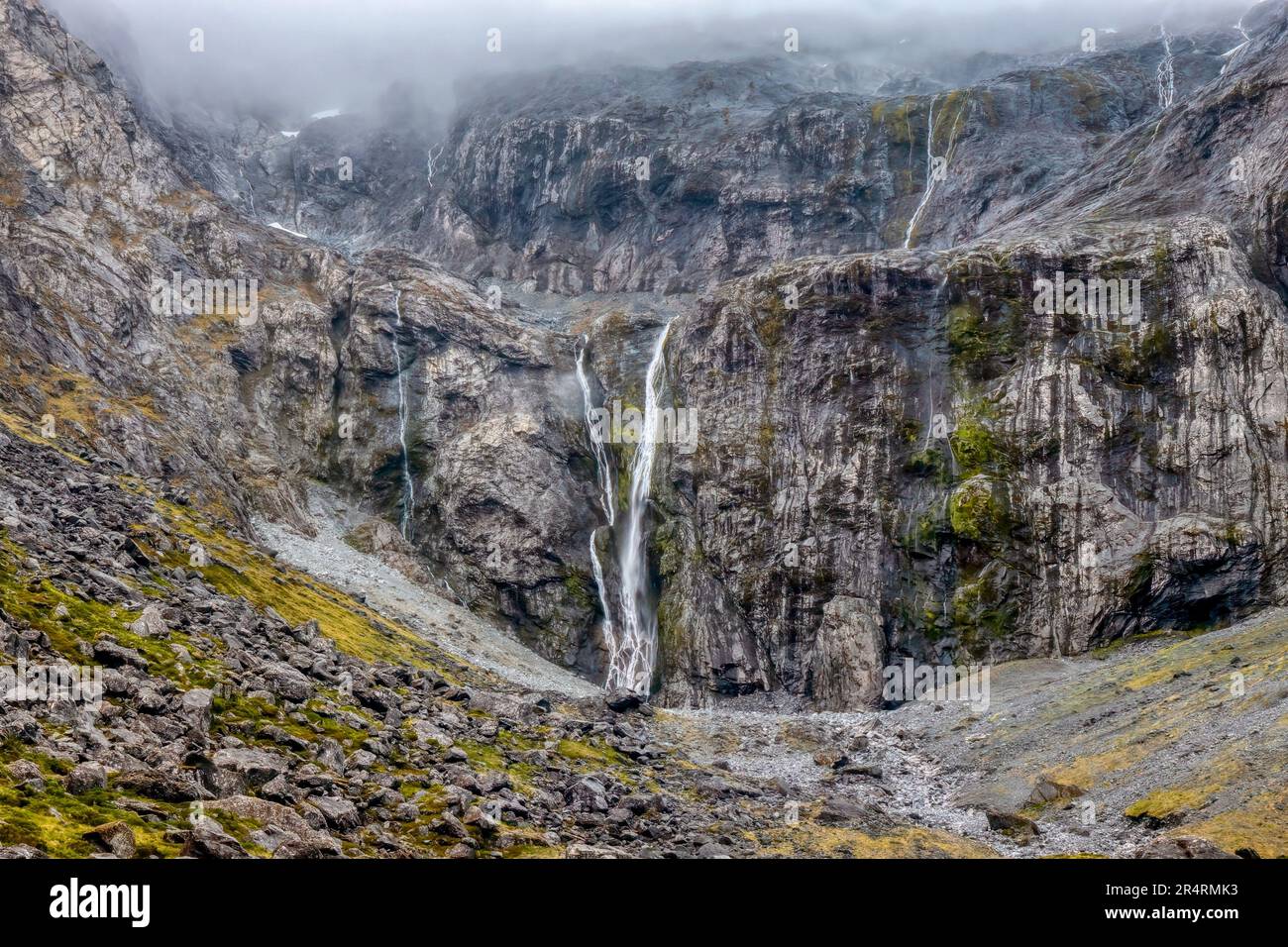 Waterfalls, mist and rain over a steep wall of granite on the South Island of New Zealand, near ...