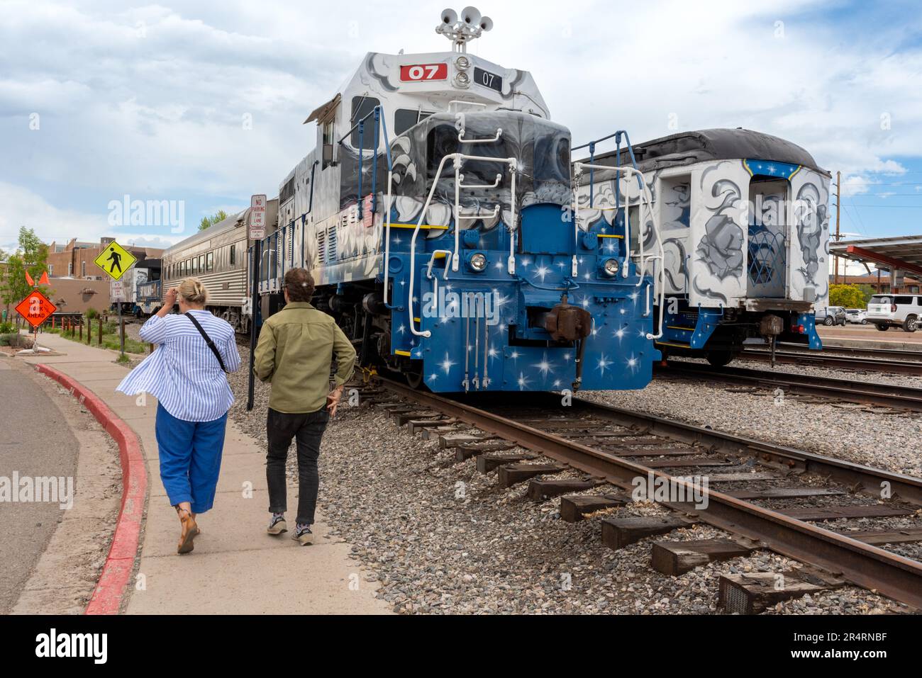 Tourists, a man and woman, walk towards brightly painted train cars ...
