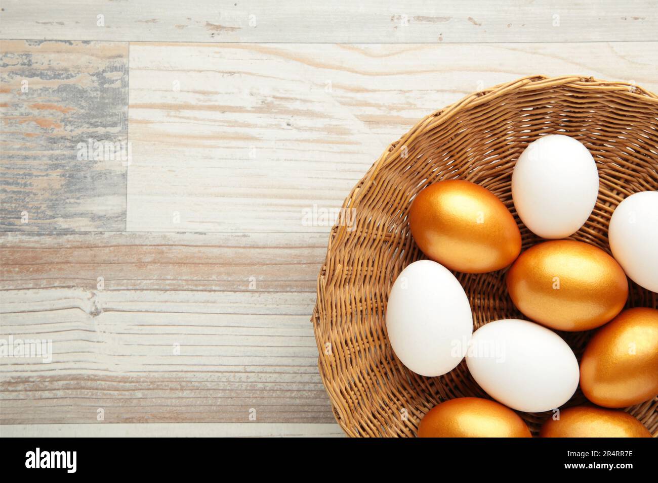 Gold and ordinary eggs in the basketon on light wooden bacground. Top ...