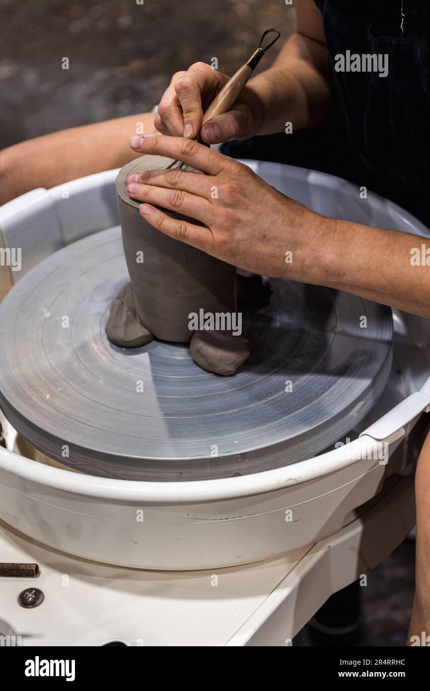 Woman working on a pottery wheel shaping and trimming a piece of dried ...