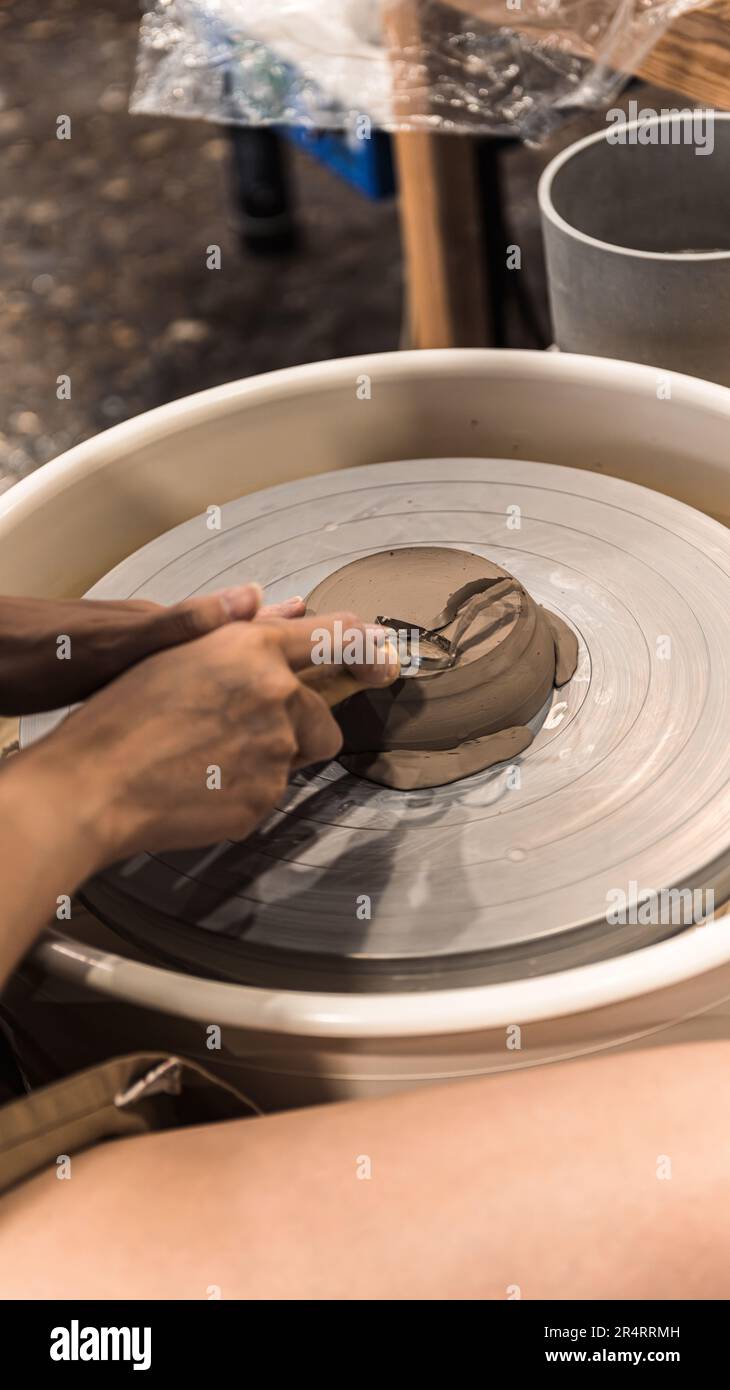 Woman working on a pottery wheel shaping and trimming a piece of dried ...
