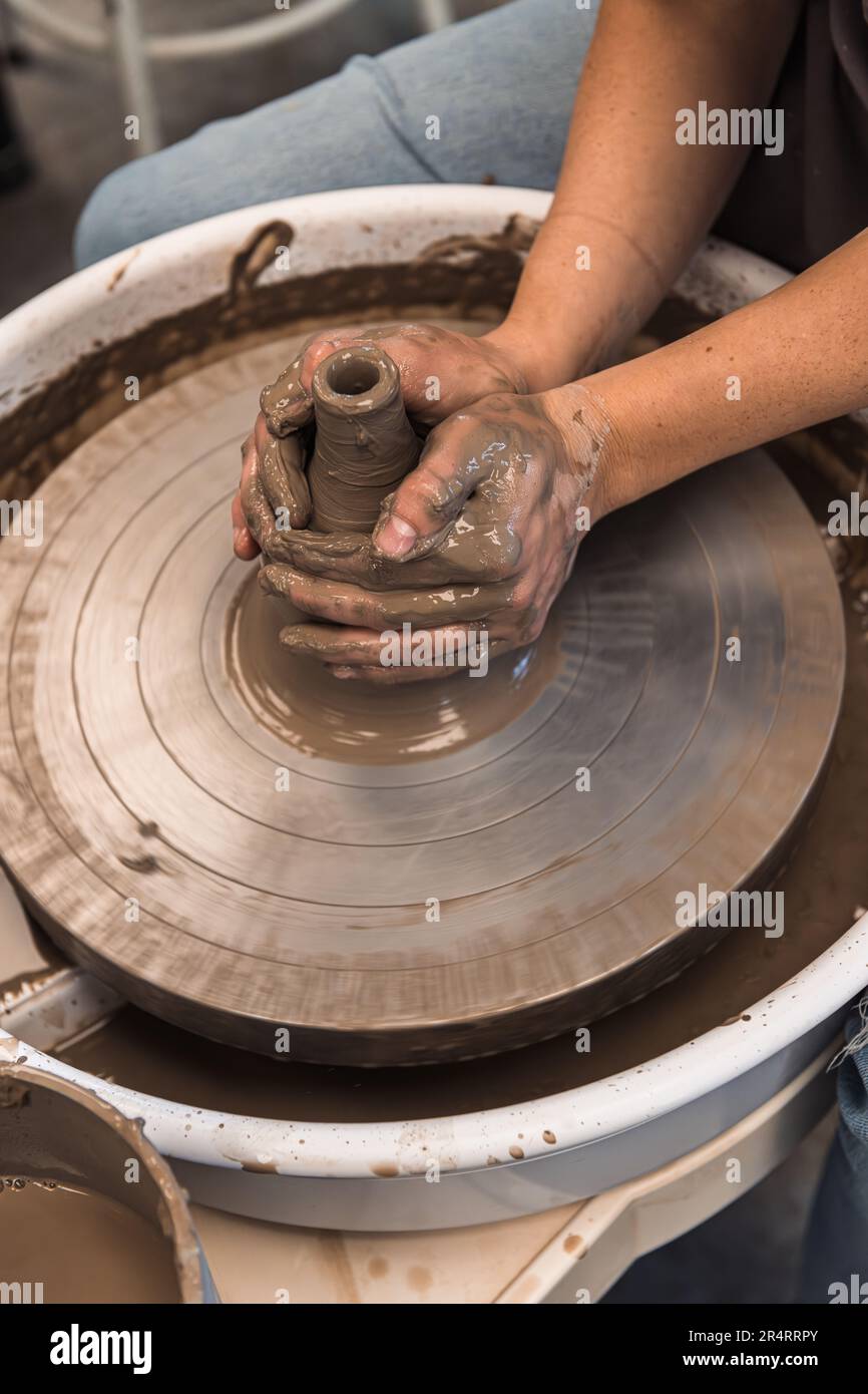 Woman working on a pottery wheel shaping the brown clay with both hands ...