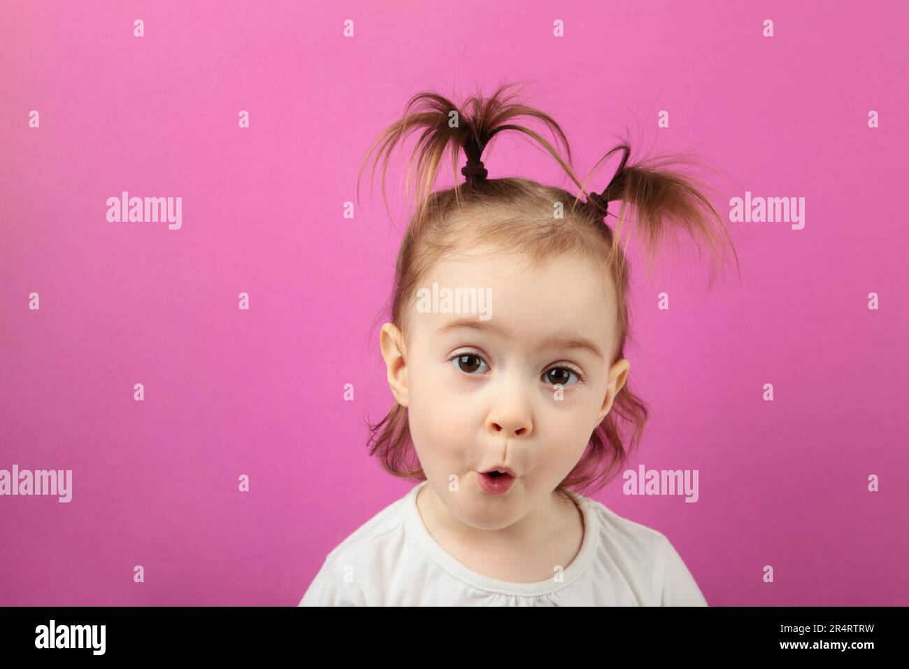 Portrait of surprised cute little girl standing on pink background. Top ...