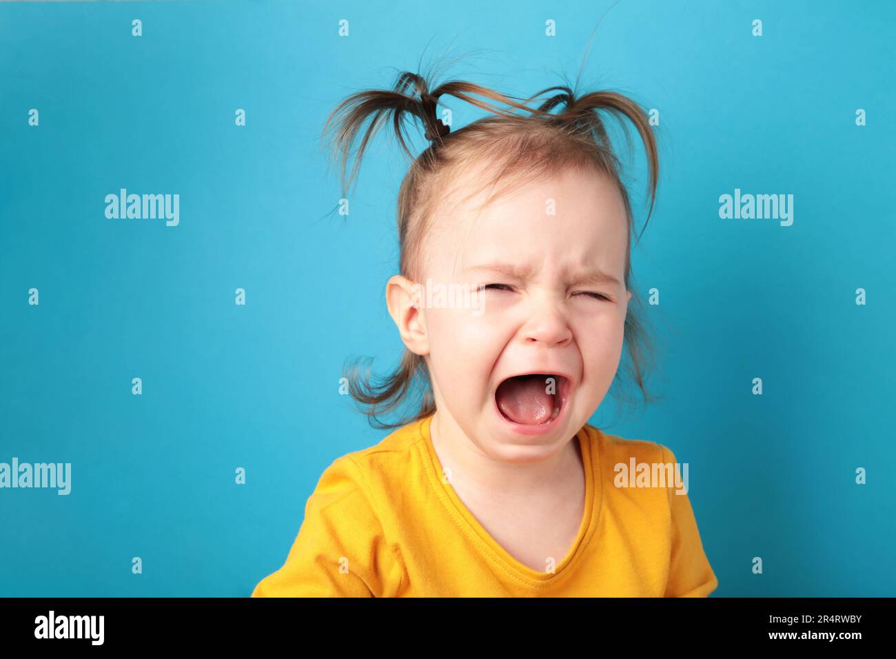 Upset little baby girl crying on blue background Stock Photo - Alamy