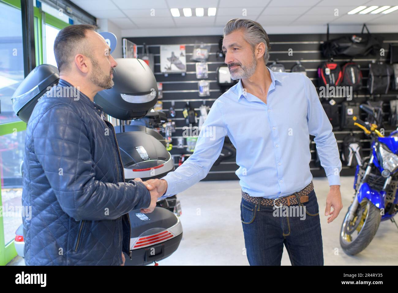 motorcycle dealer shaking hands with customer entering shop Stock Photo ...