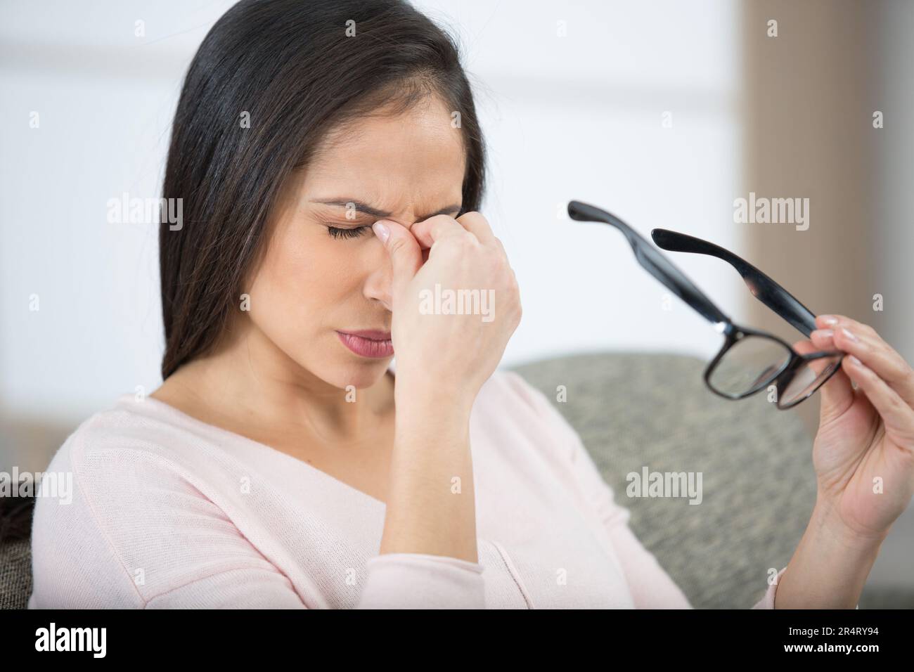 woman holding glasses to rub the bridge of her nose Stock Photo - Alamy