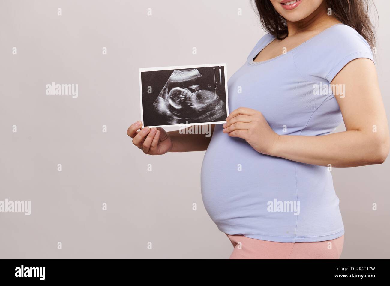 Close-up belly of a smiling pregnant woman holding ultrasound scan ...