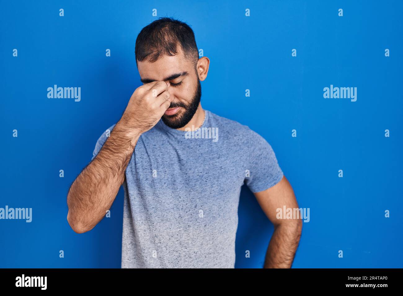 Middle east man with beard standing over blue background tired rubbing ...