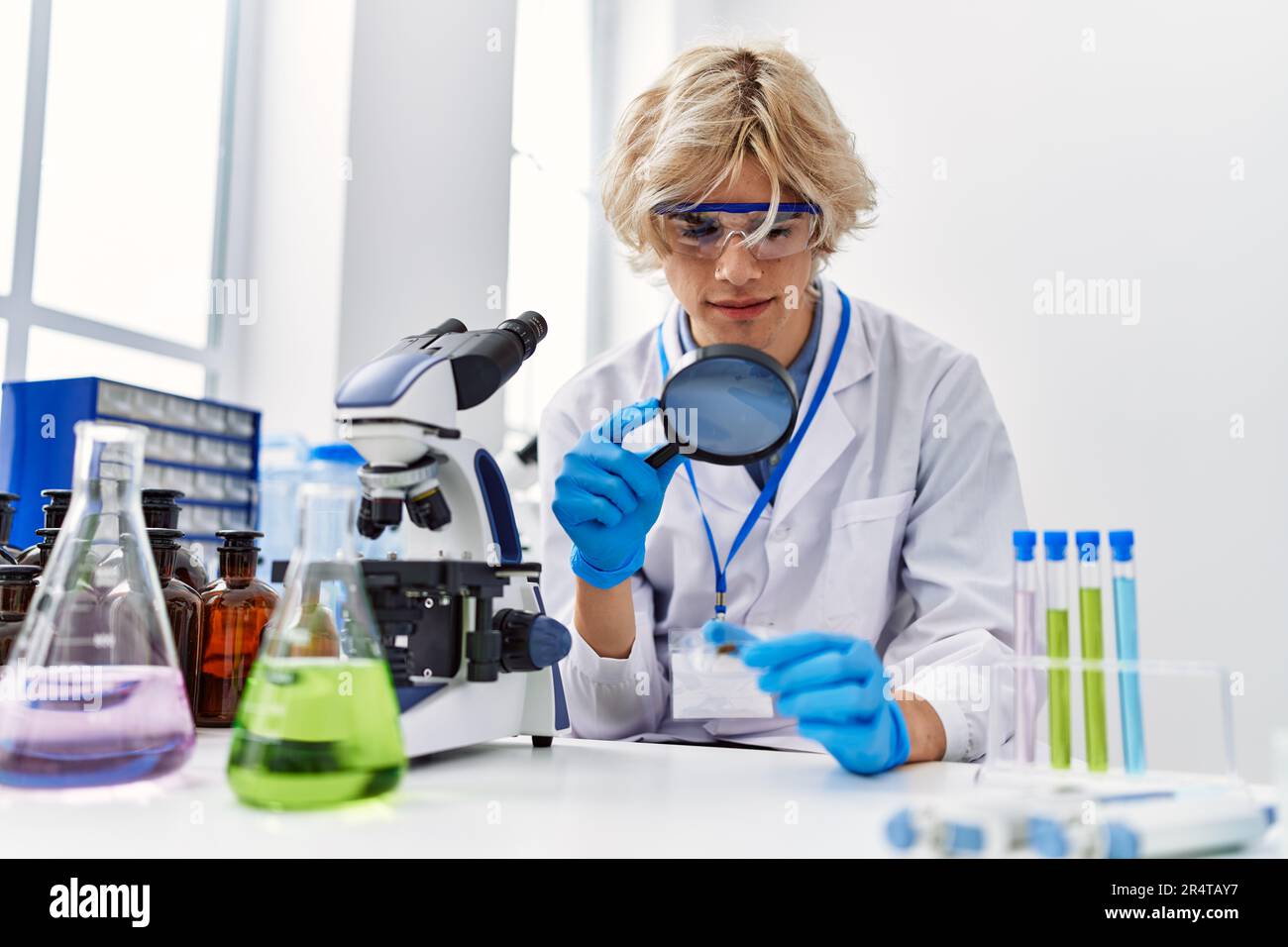 Young blond man scientist using magnifying glass at laboratory Stock ...