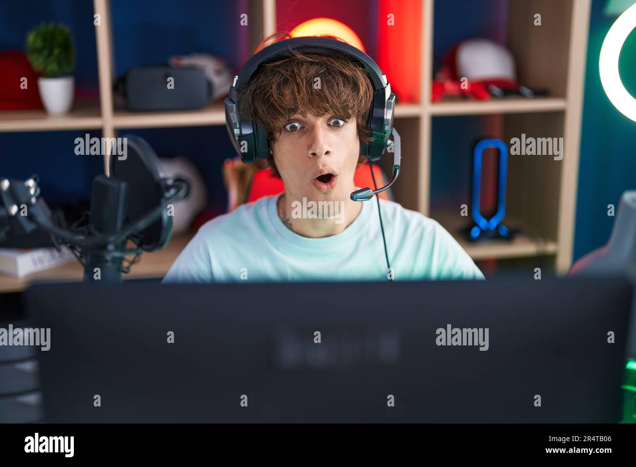 Hispanic young man playing video games scared and amazed with open ...