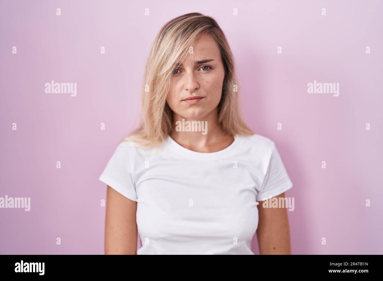 Young blonde woman standing over pink background skeptic and nervous ...