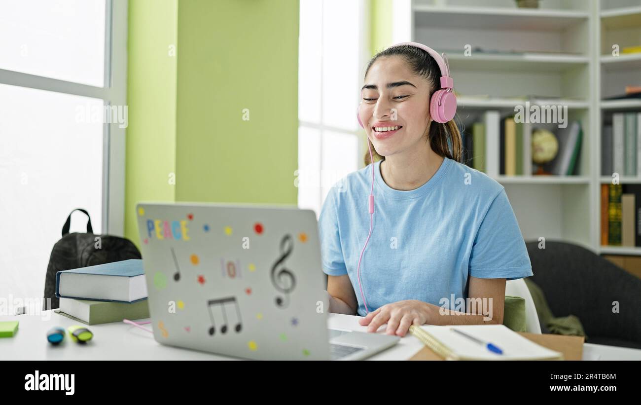 Young beautiful hispanic woman student using laptop and headphones ...