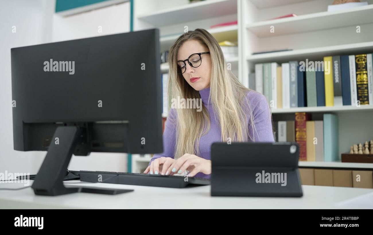 Young blonde woman student using computer and touchpad studying at ...