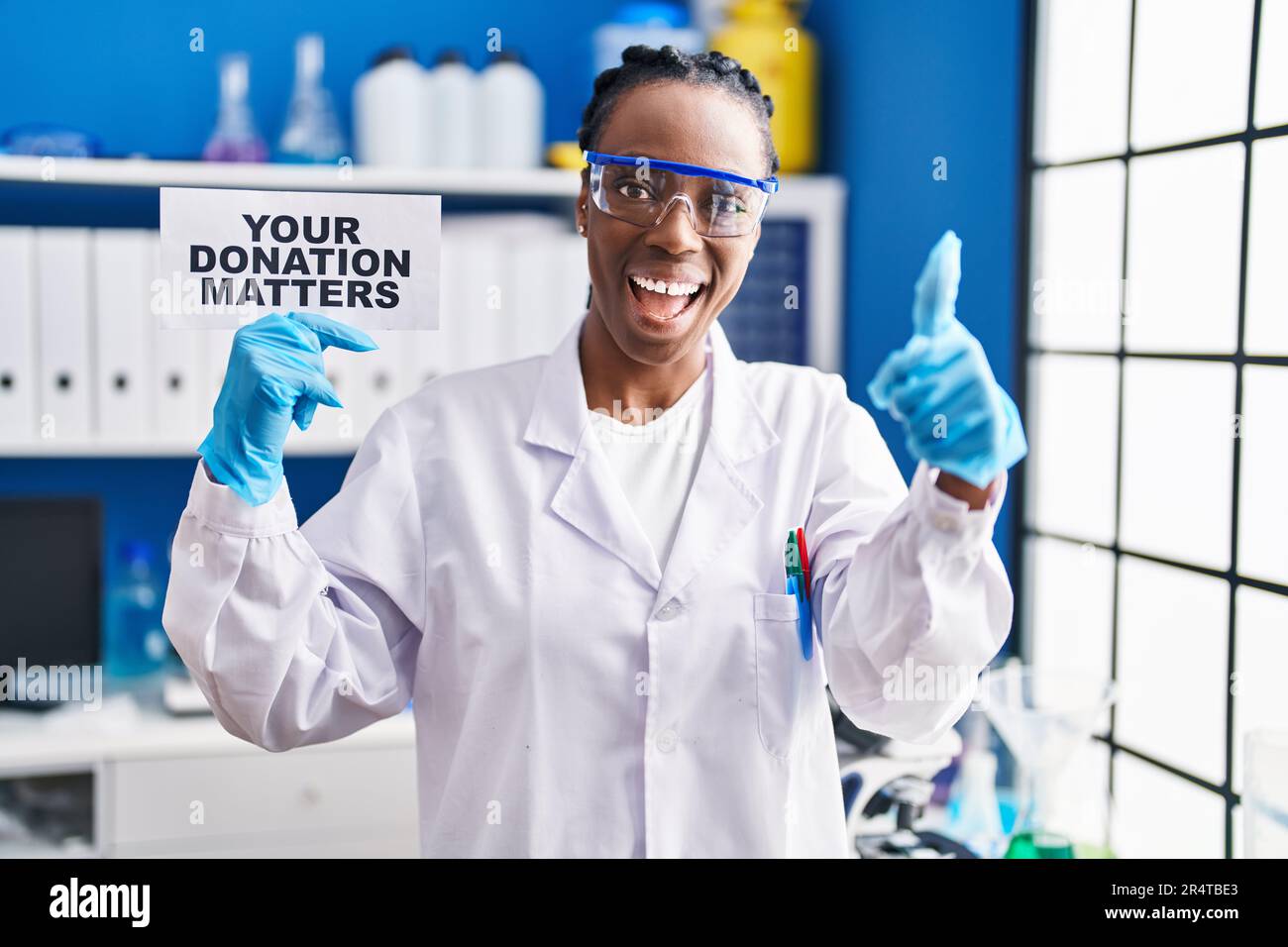 Beautiful black woman working at scientist laboratory holding your donation matters banner ...