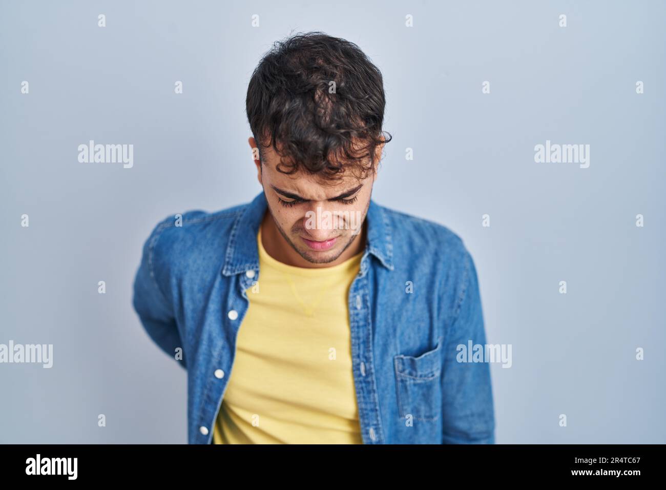 Young hispanic man standing over blue background suffering of backache ...