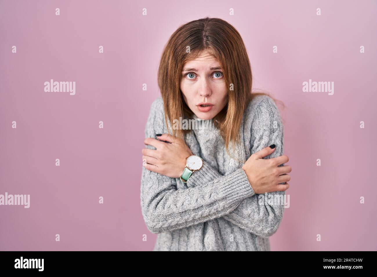 Beautiful woman standing over pink background shaking and freezing for ...