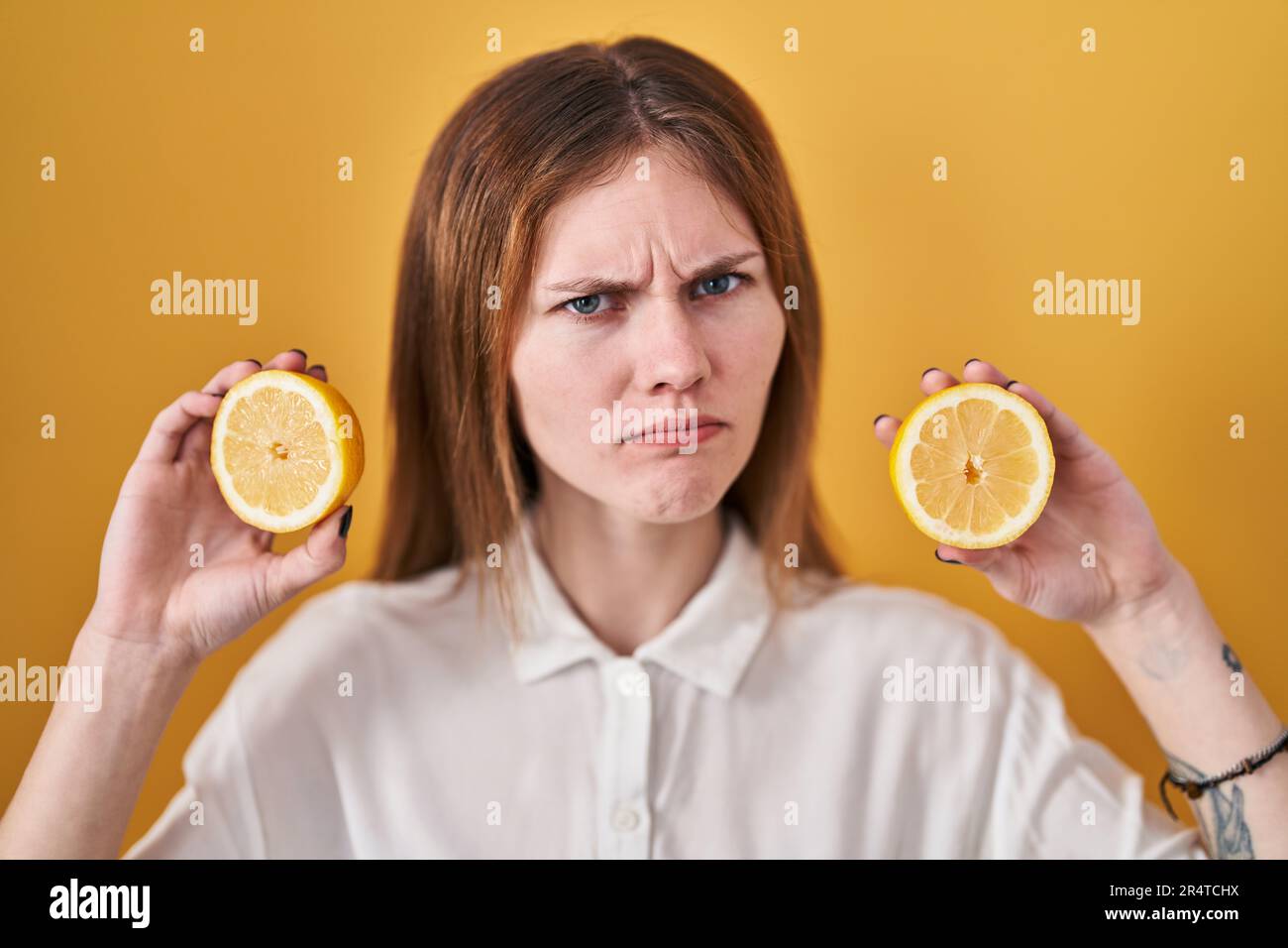 Beautiful woman holding lemons skeptic and nervous, frowning upset ...