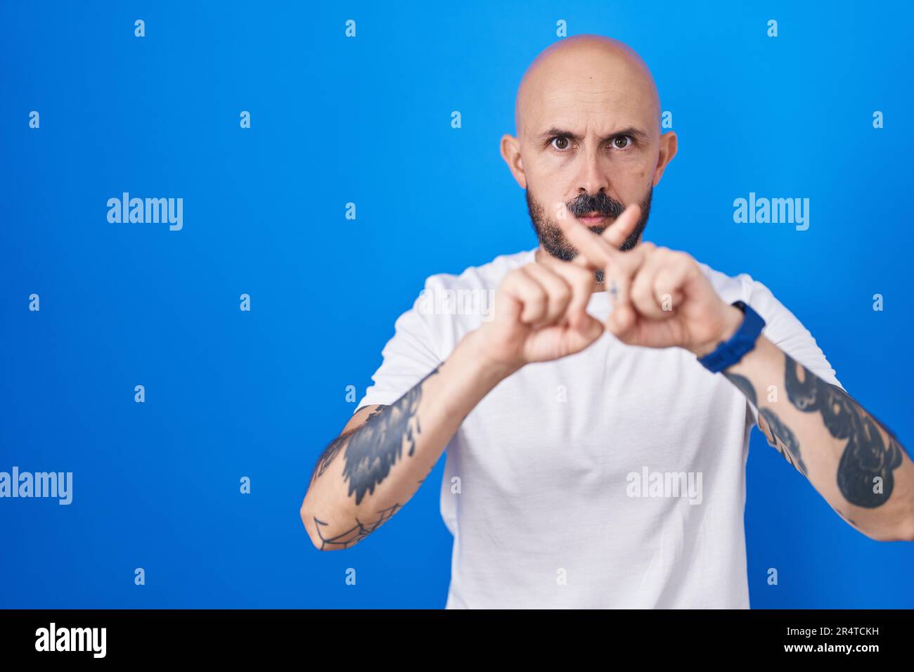 Hispanic man with tattoos standing over blue background rejection ...