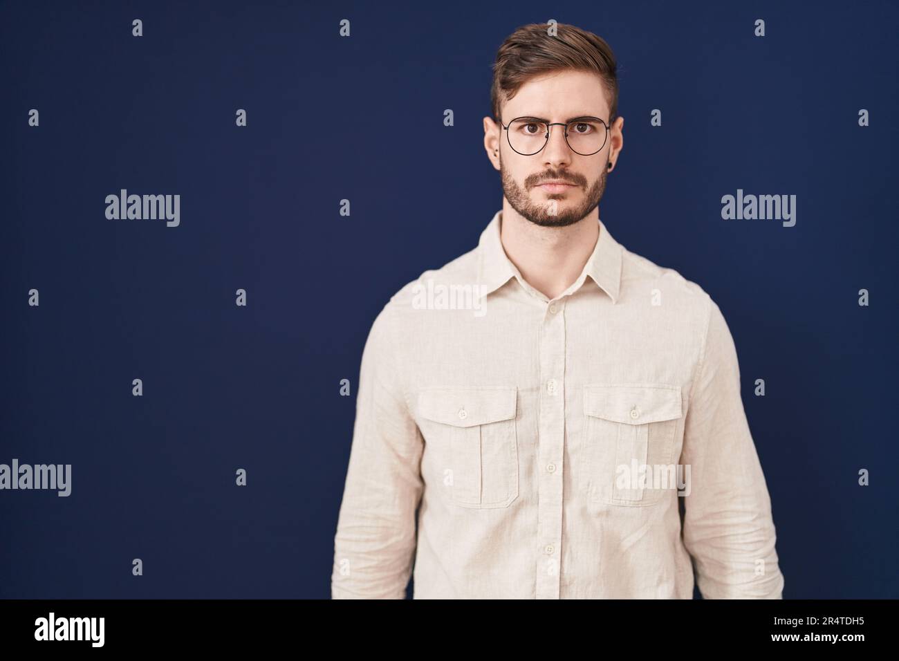 Hispanic man with beard standing over blue background relaxed with ...