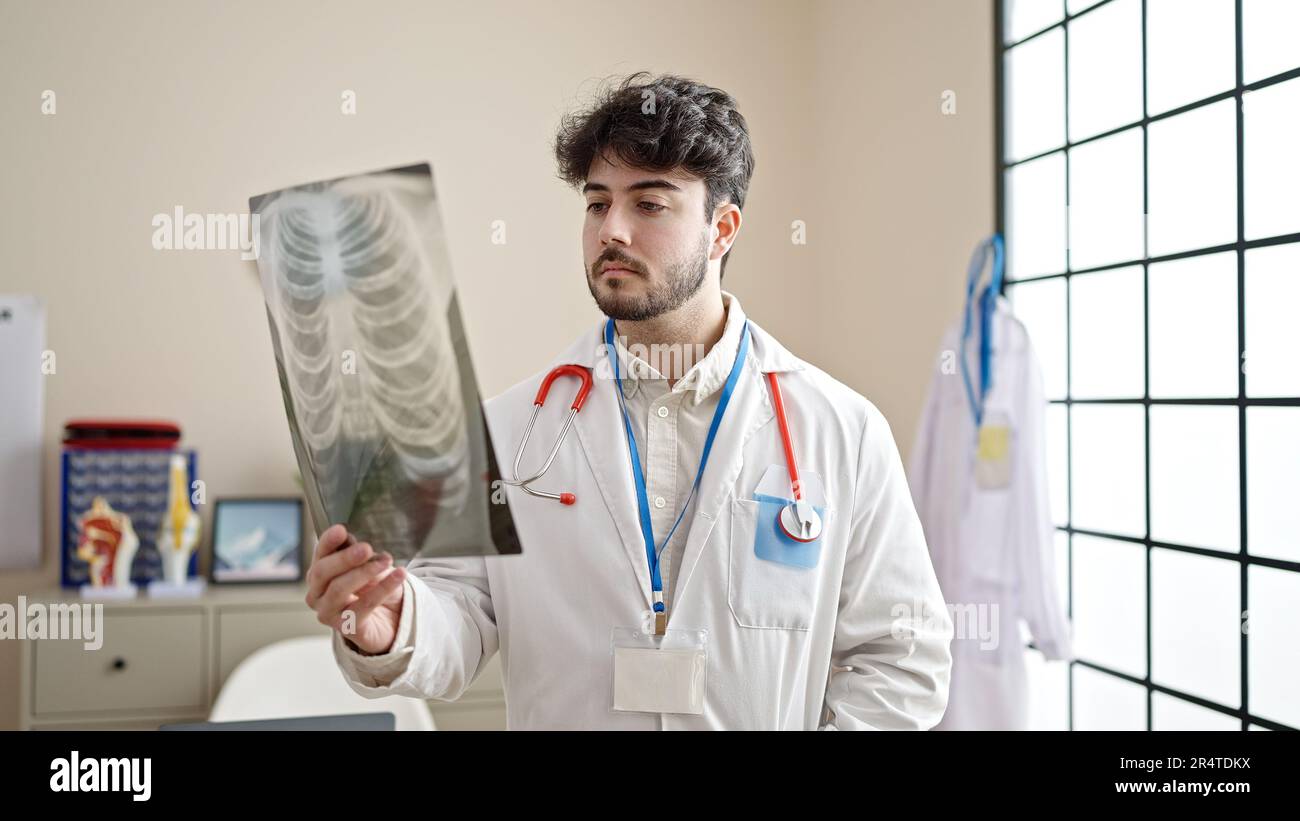 Young hispanic man doctor standing with doubt expression¡ looking xray ...