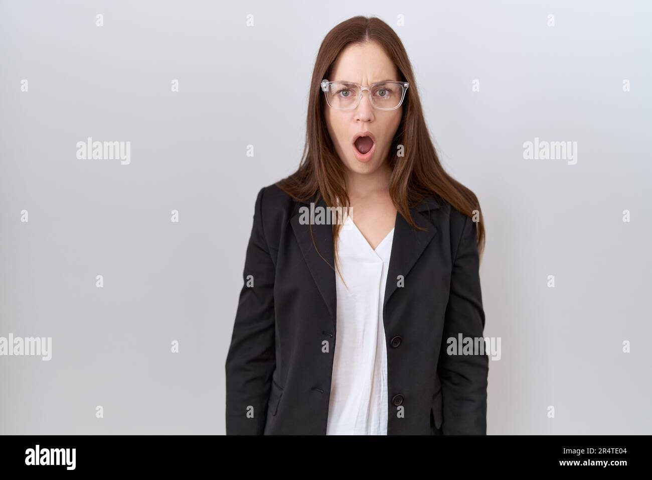 Beautiful brunette woman wearing business jacket and glasses in shock ...
