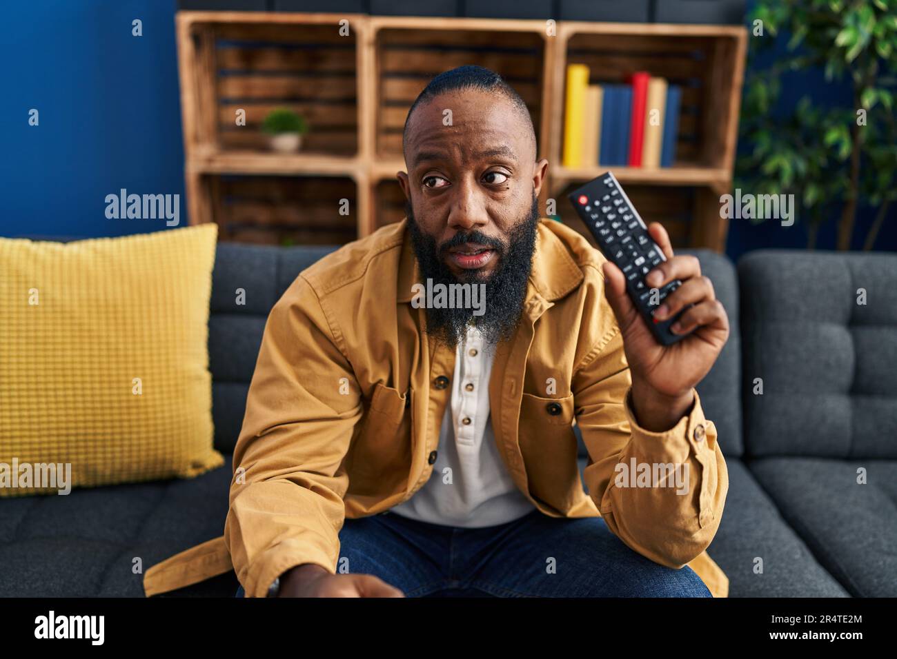 African american man holding television remote control scared and ...